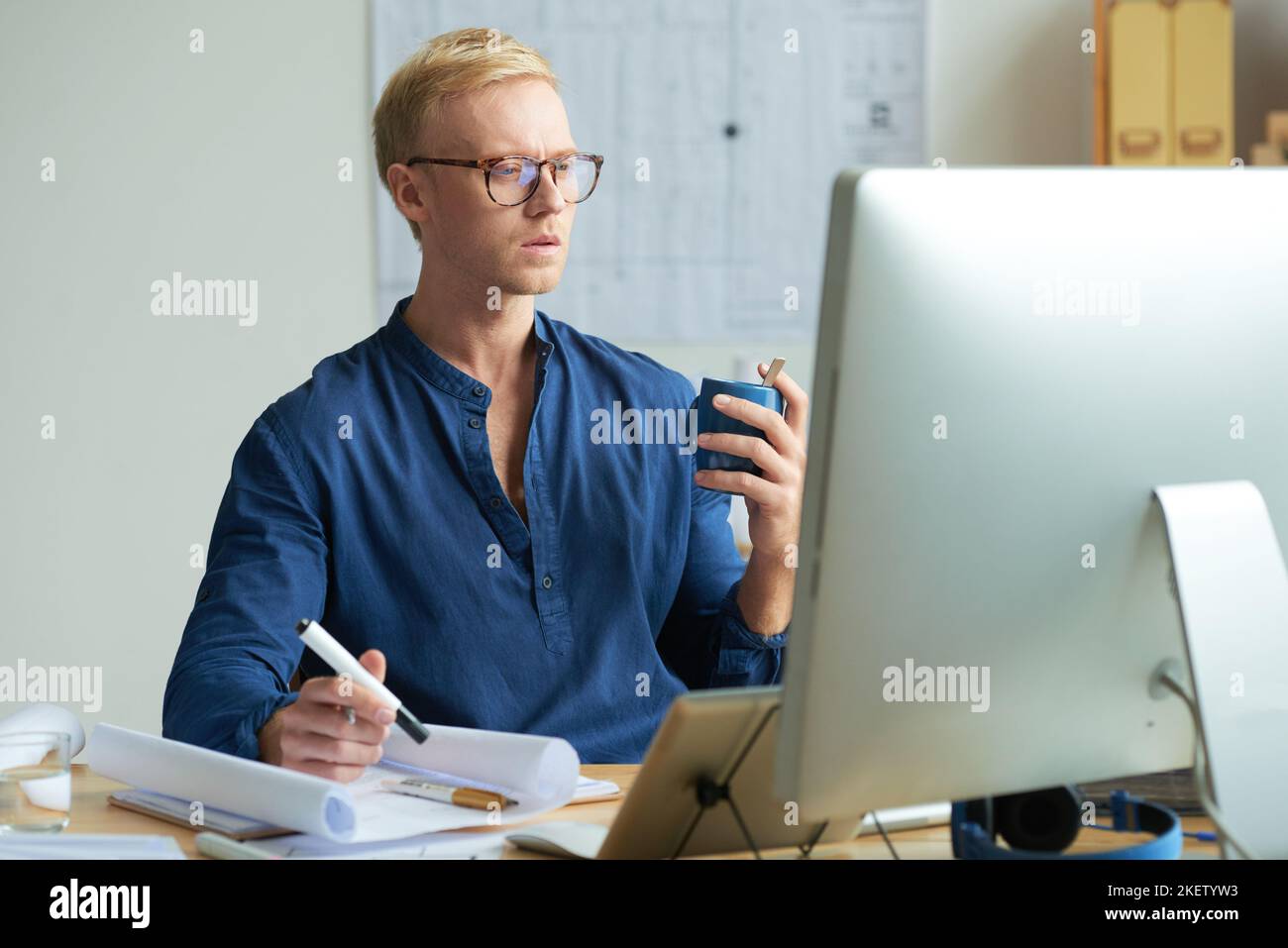 Creative man drinking coffee and examining construction plan on ...