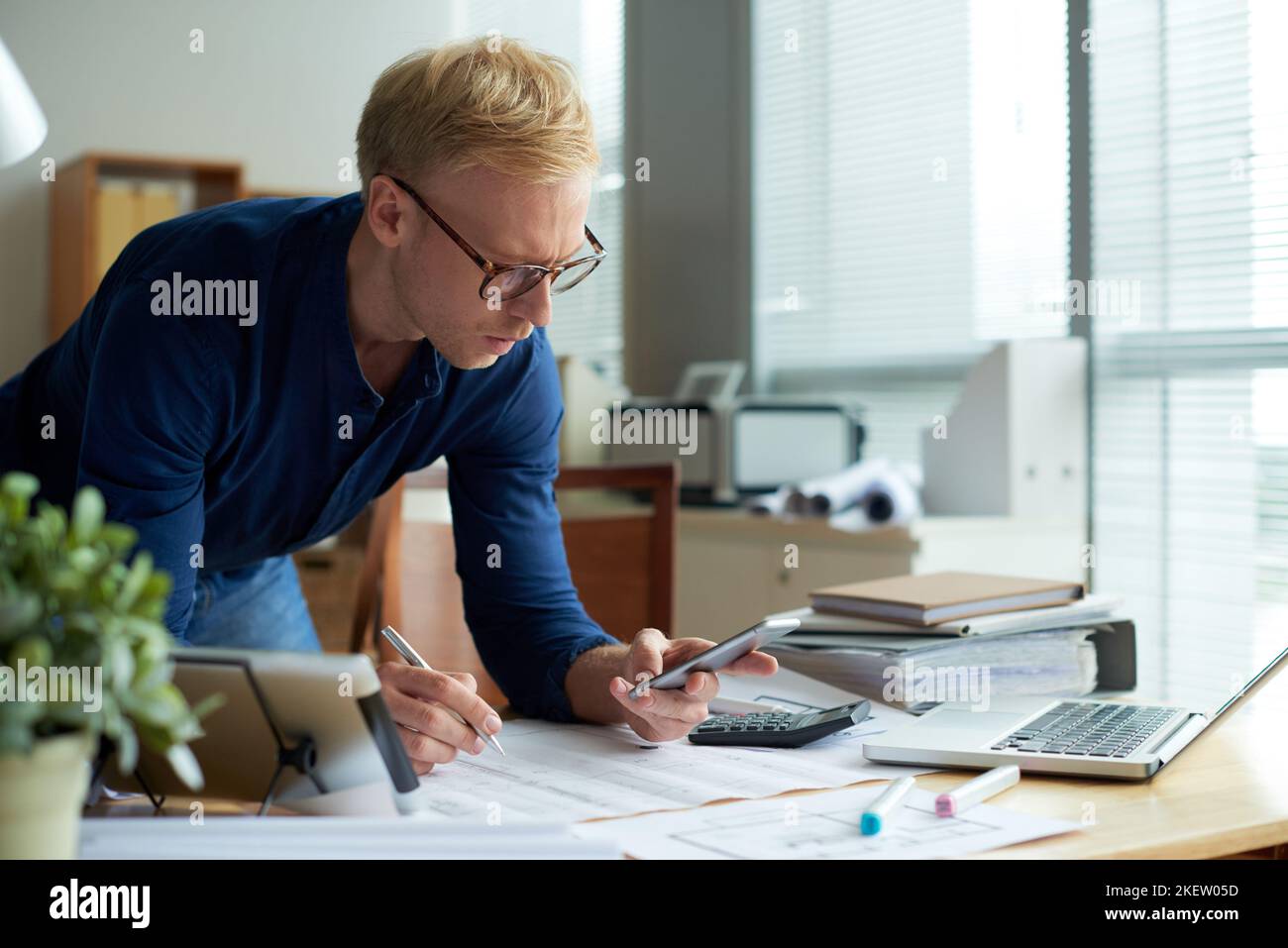 Architect checking figures in smartphone when drawing blueprint Stock ...