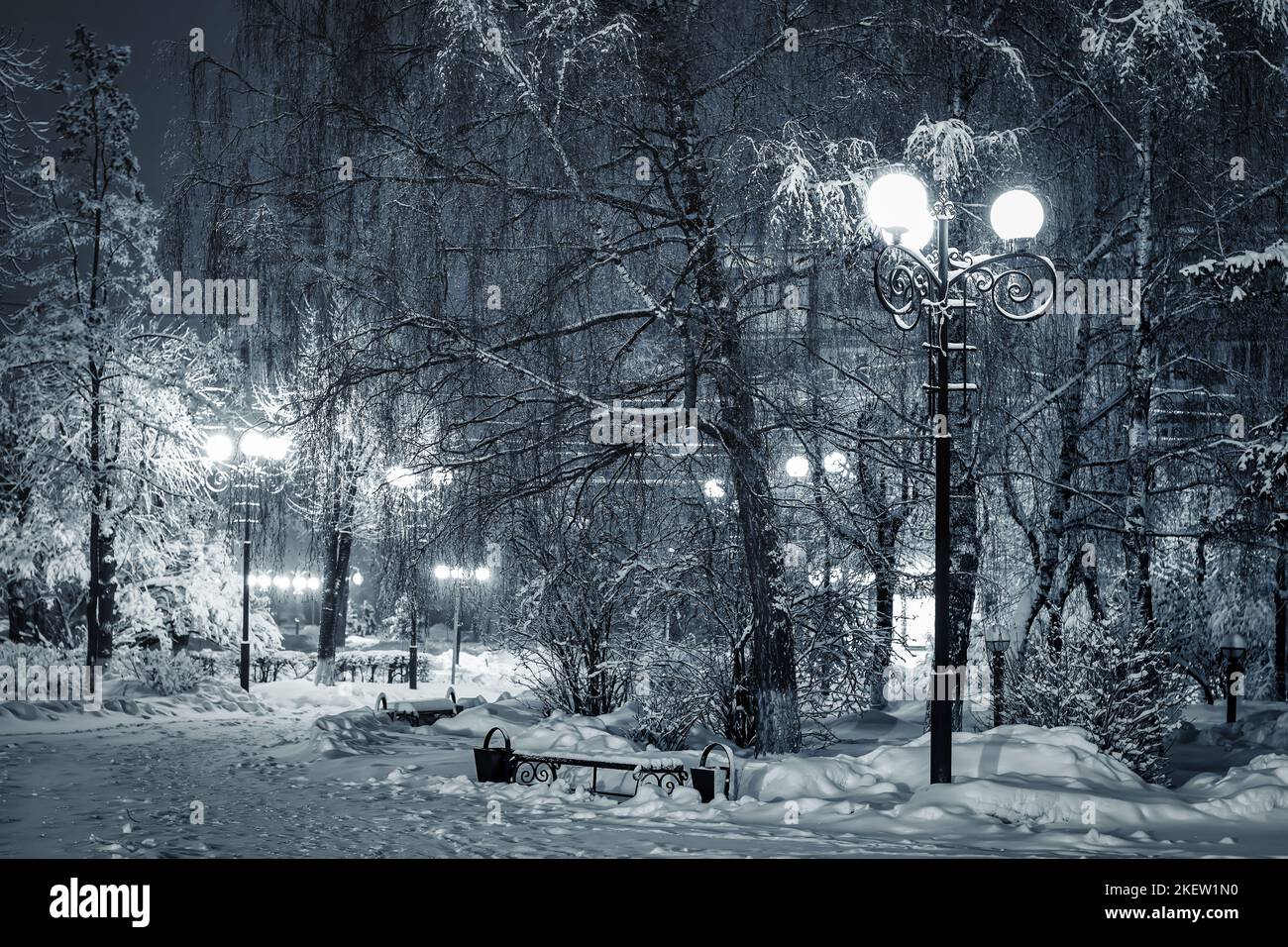 Winter park at night with glowing lanterns, pavement covered with snow ...