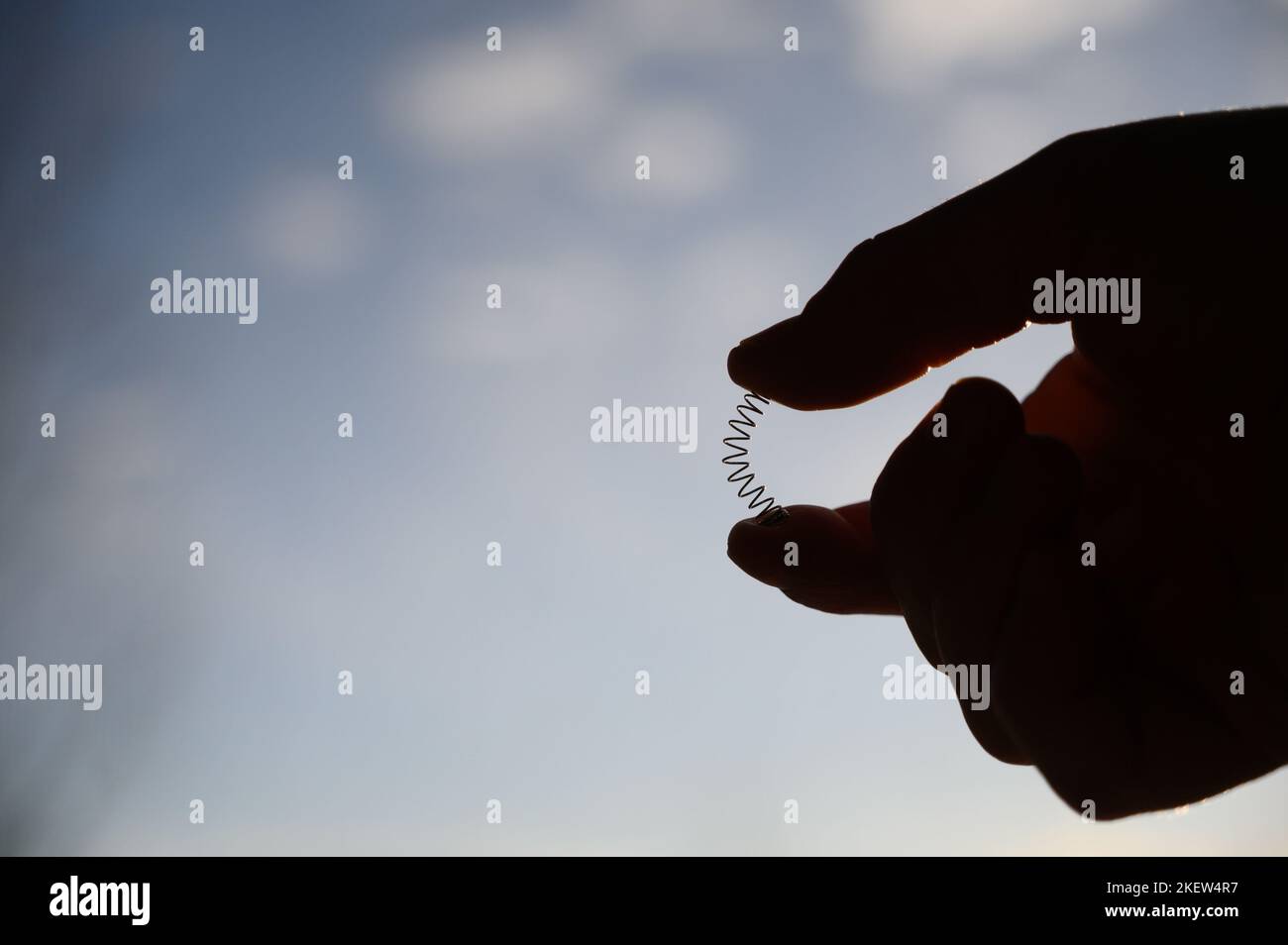 Caucasian hand compressing a metal spring between a thumb and finger ...