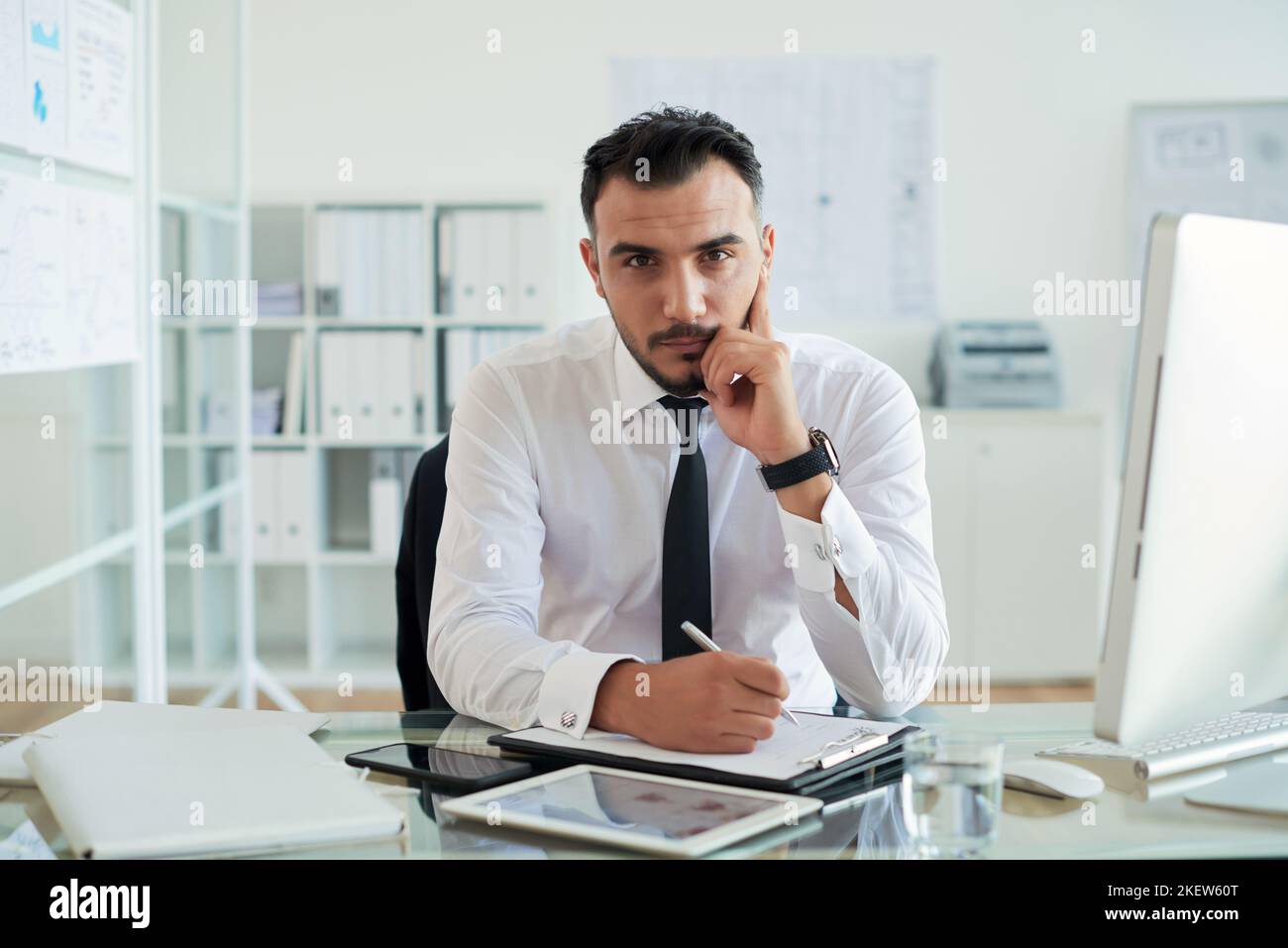 Portrait of entrepreneur sitting at his table in office and looking at ...