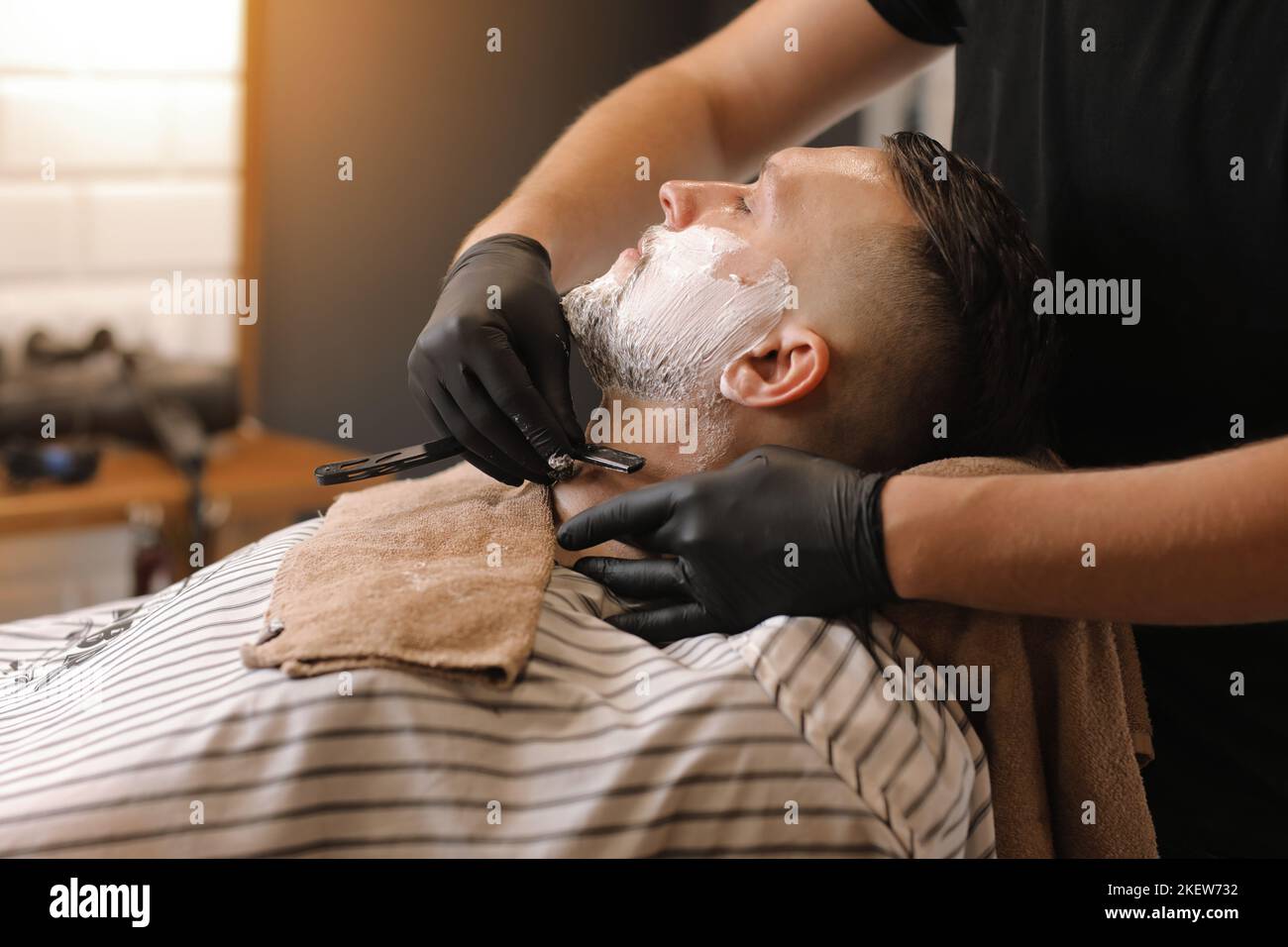 Professional barber in black gloves is shaving client with a vintage ...