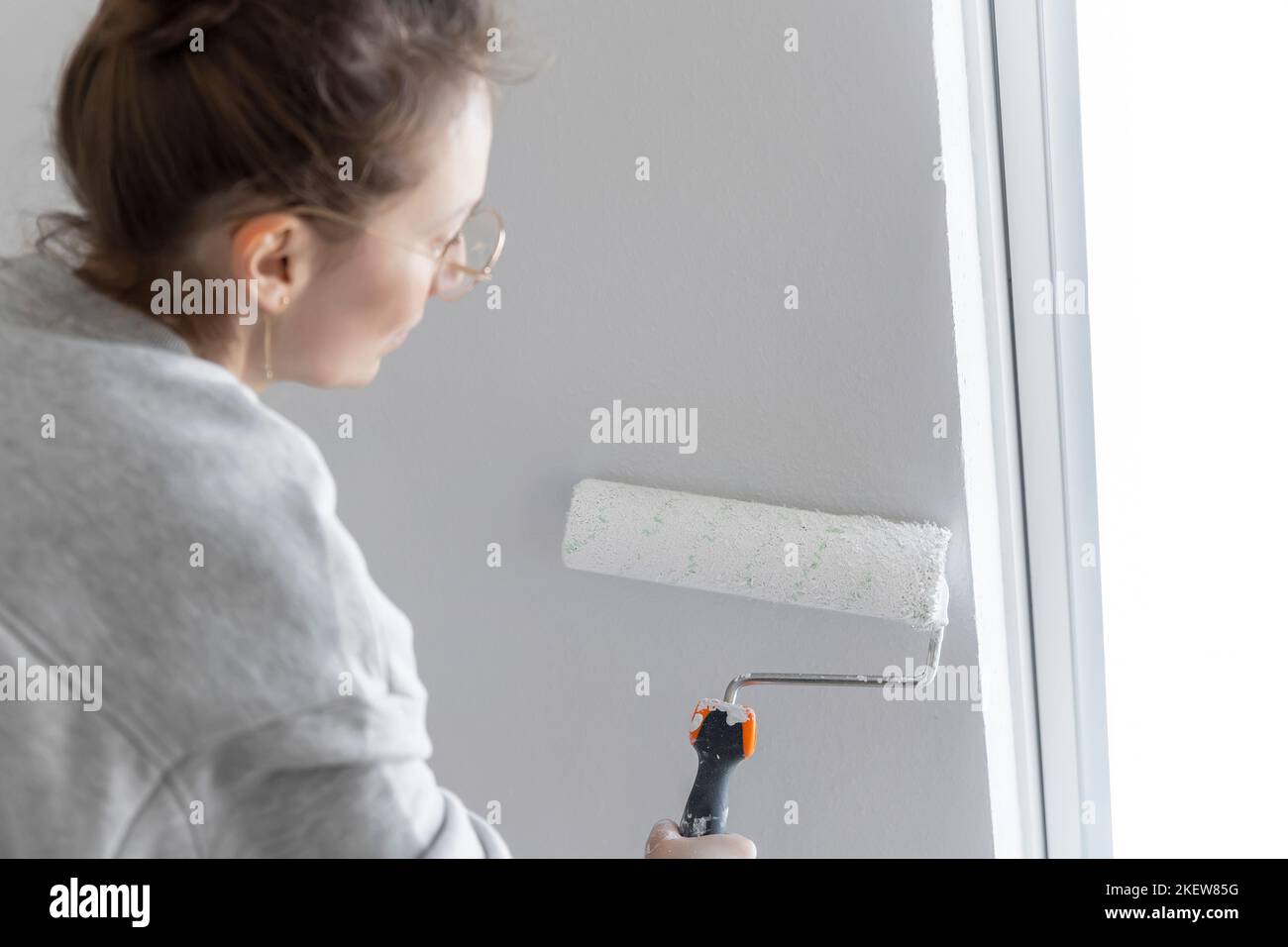 Close-up view young adult woman hand painting wall paint holding roller ...