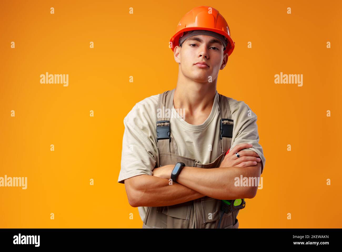 Young construction worker in helmet and uniform posing on yellow ...