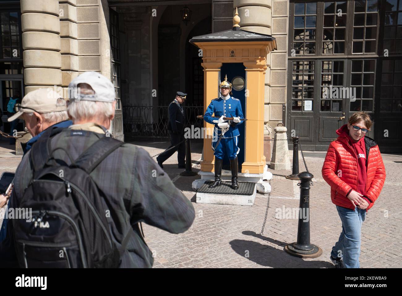 Tourists gather around a Royal Guard stood outside the Royal Palace ...