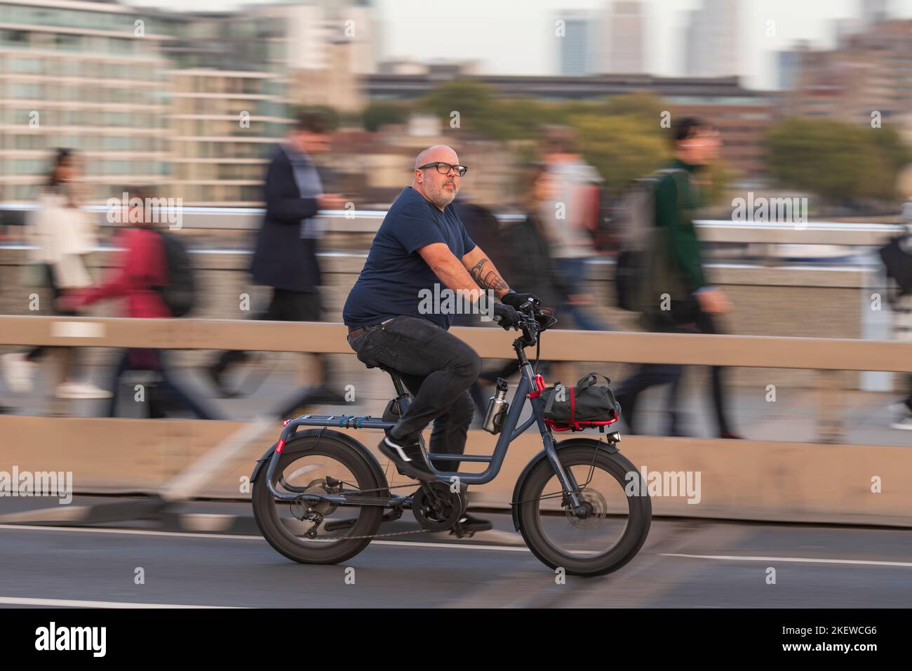 A man cycling on an e-bike during rush hour, across London Bridge, London, UK. 18 Oct 2022 Stock ...