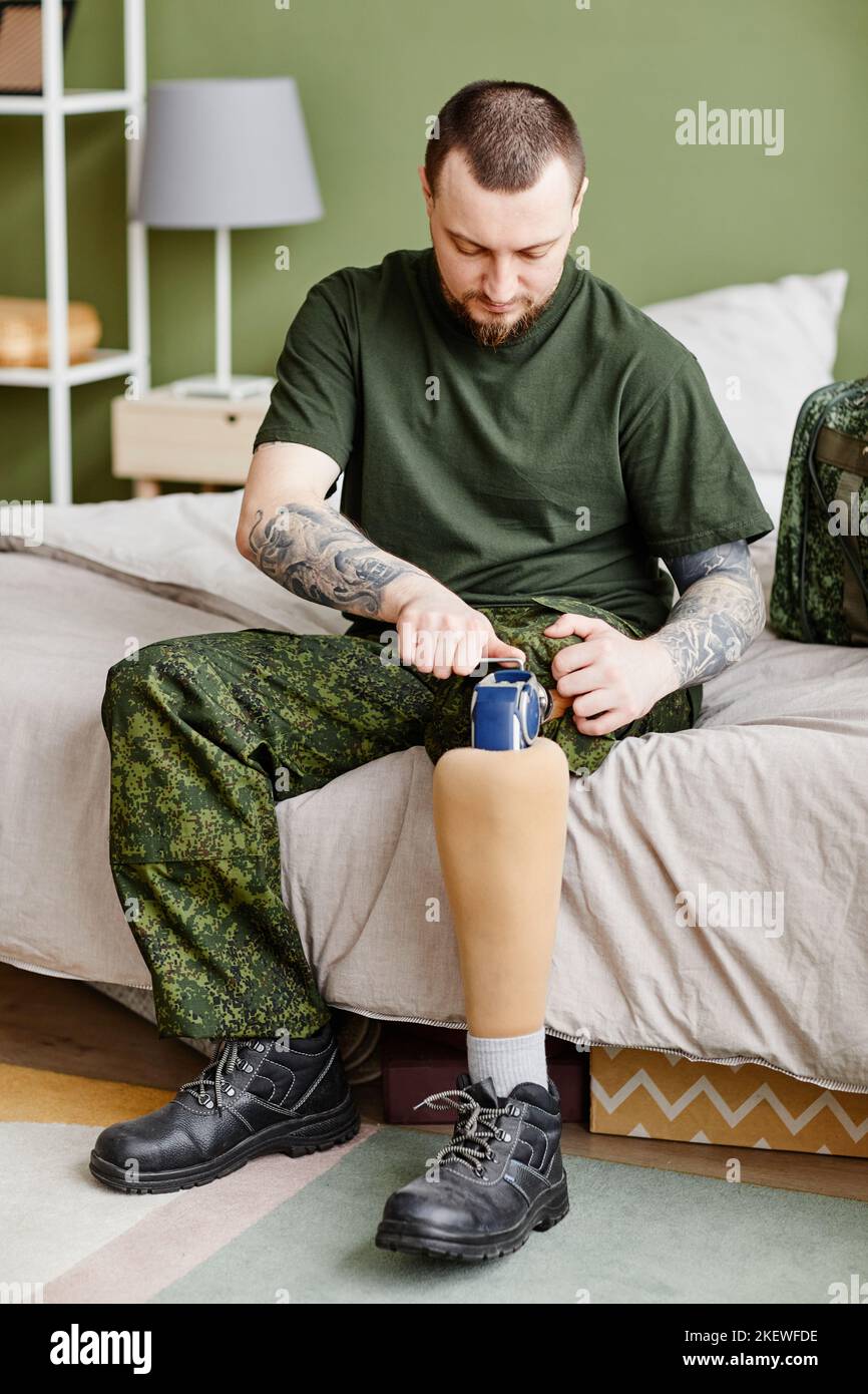 Vertical full length portrait of military veteran fixing prosthetic leg ...