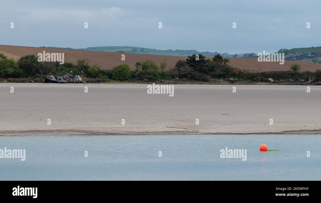 A orange buoy on a calm water surface. The sandy shore of the sea bay ...