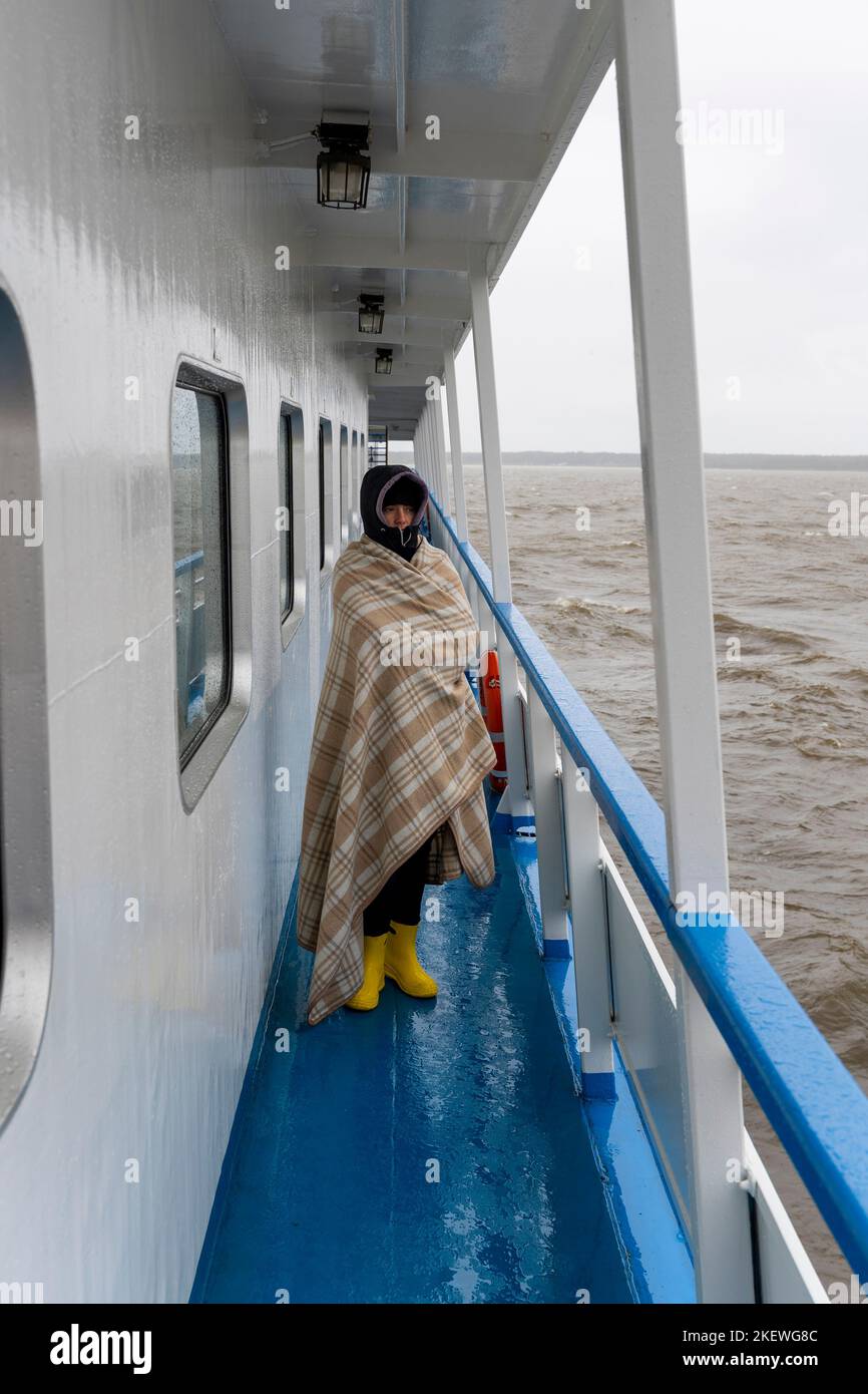 woman wrapped in a plaid walks along the side of a ship sailing on sea ...