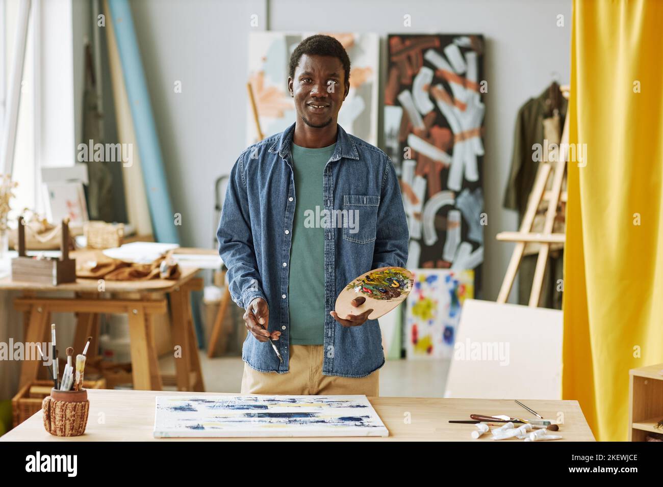 Young successful African American male artist in casualwear holding ...