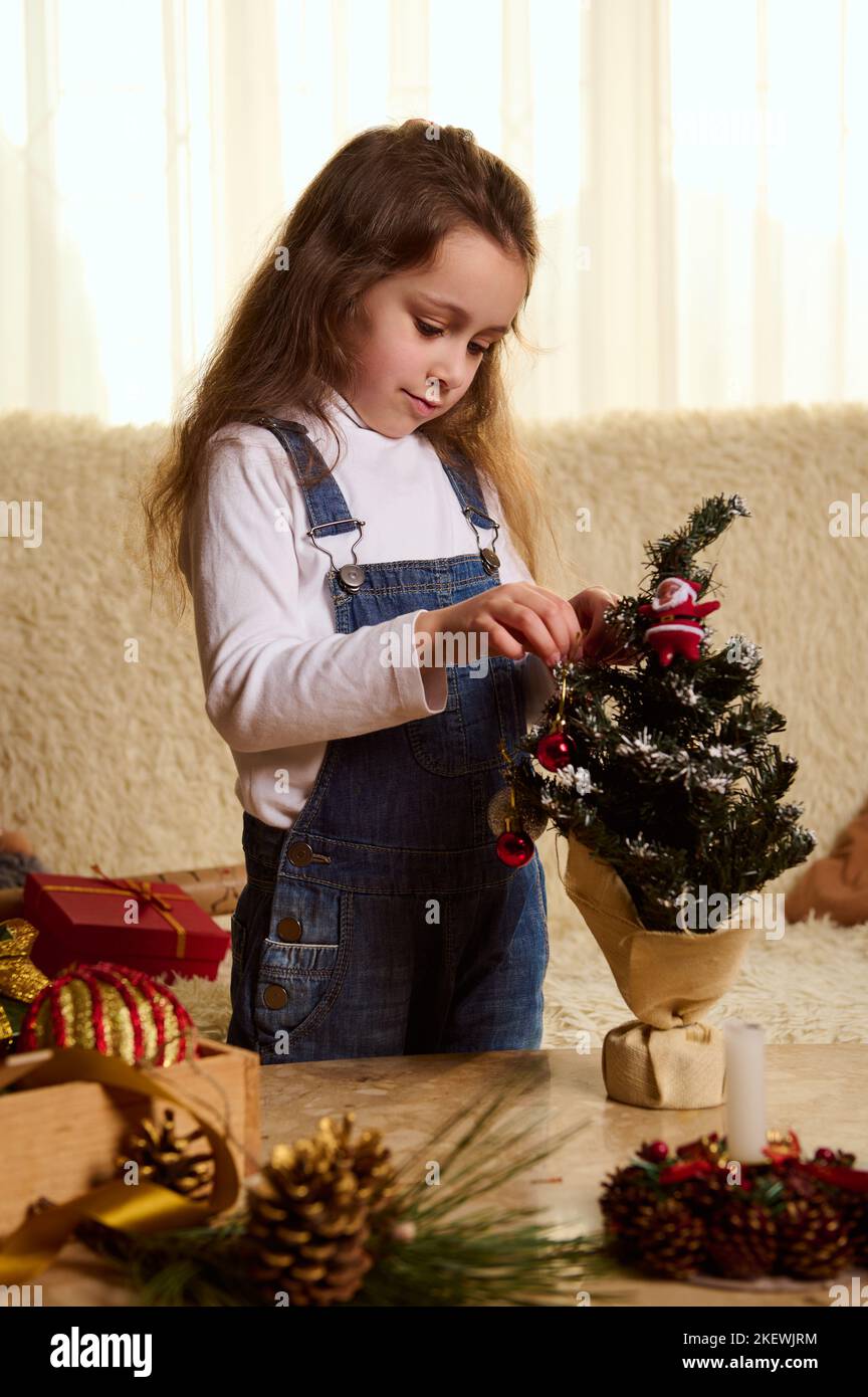 Adorable little girl enjoys New years preparations, decorates a small ...
