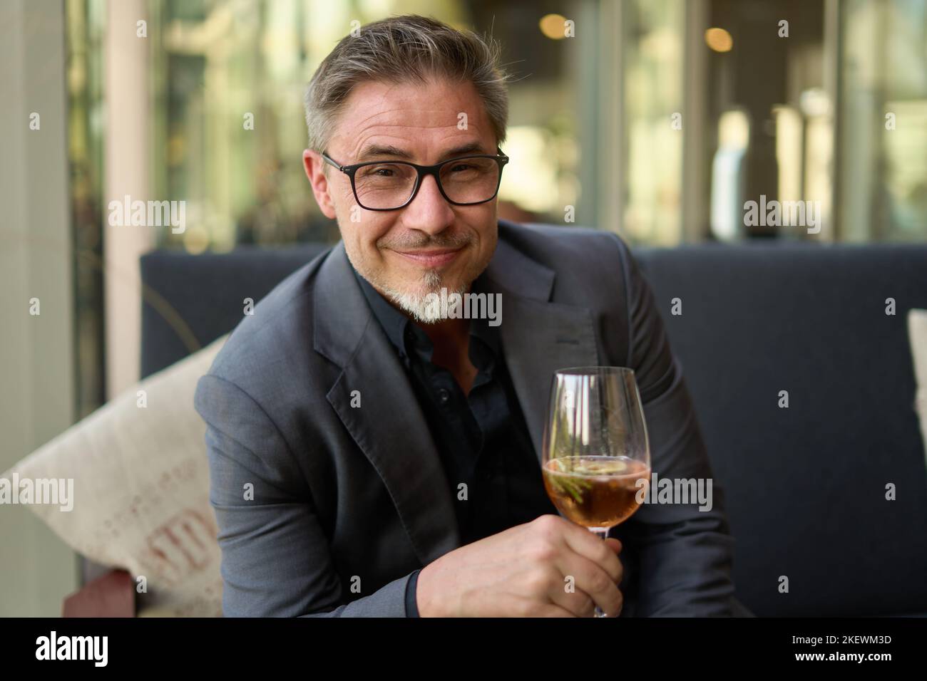 Older man sitting on coach drinking champagne based cocktail from wine ...