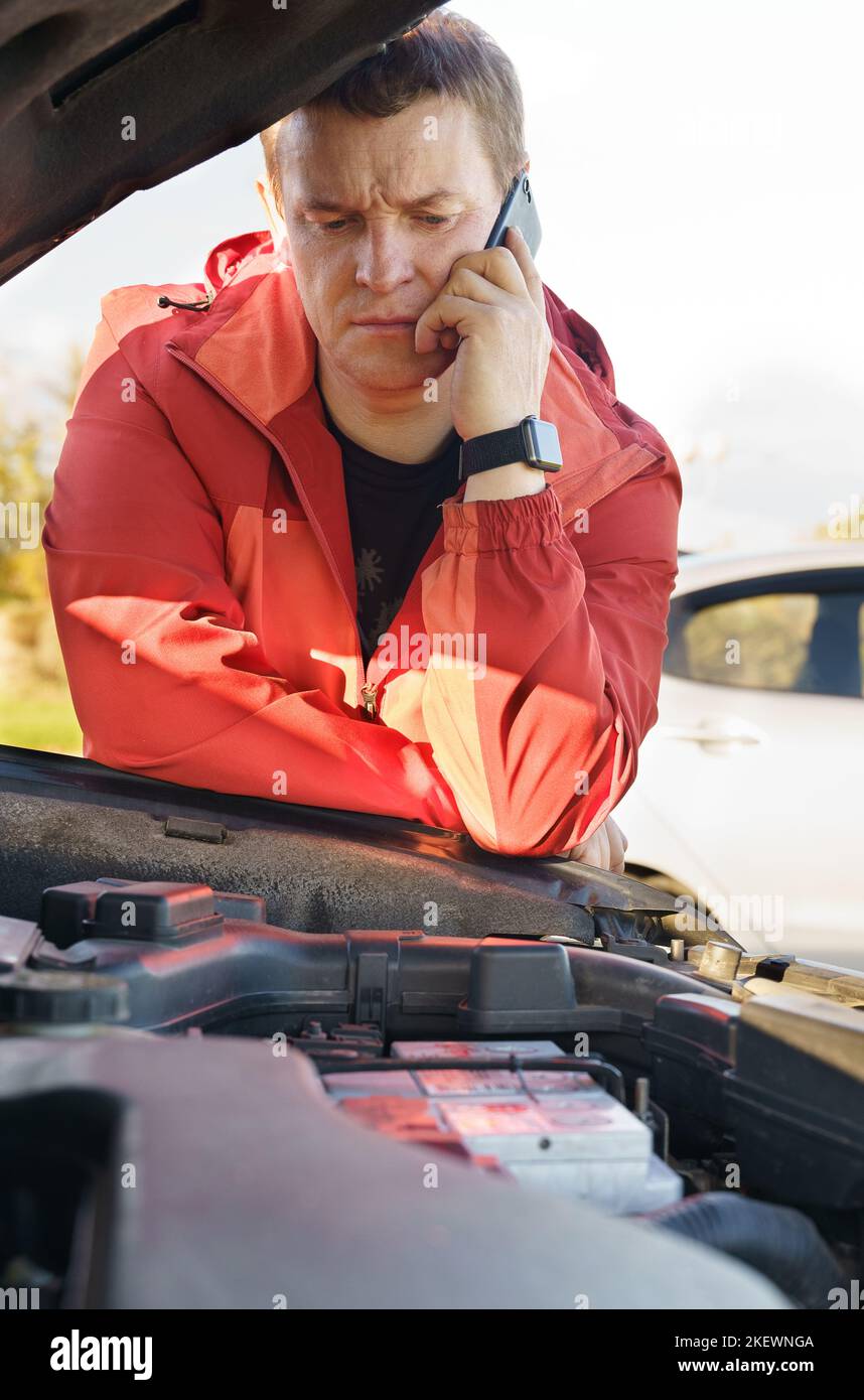 A male driver stands near the engine compartment of the car, calls the ...