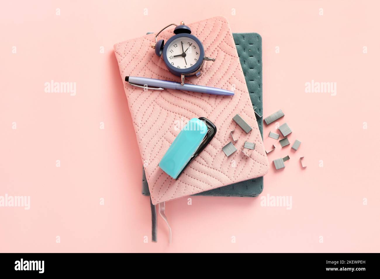 Stapler, staples, pen, notebooks and alarm clock on pink background ...