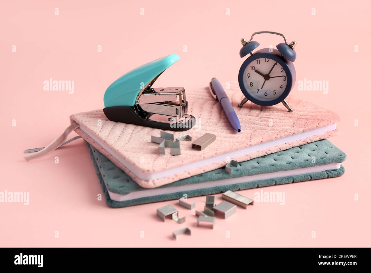 Stapler, staples, pen, notebooks and alarm clock on pink background ...