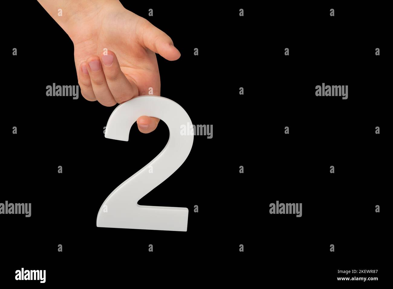 Close-up hand holding a white number 2 on a black background. Number ...