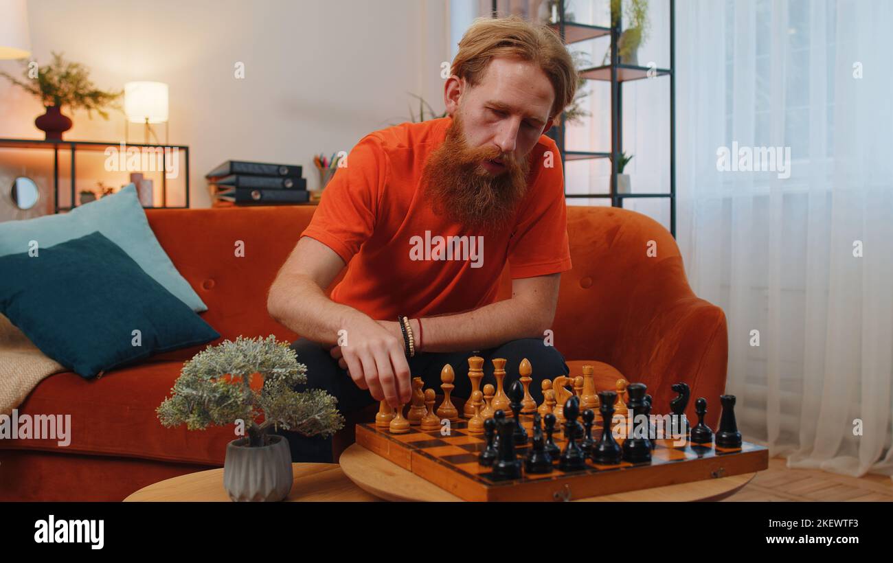 Focused caucasian bearded man chessman sitting at home room couch ...