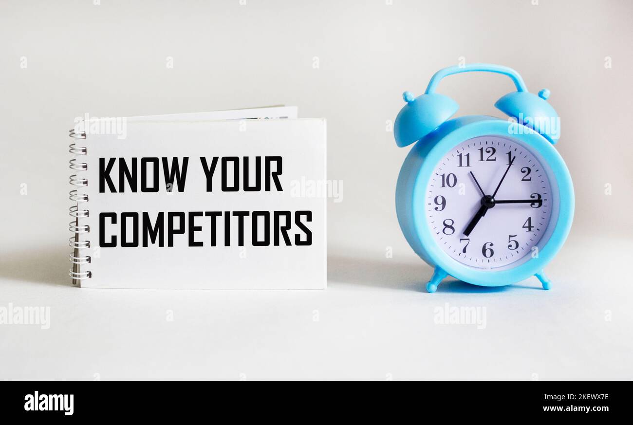 Notepad with text KNOW YOUR COMPETITORS with clock on white background ...