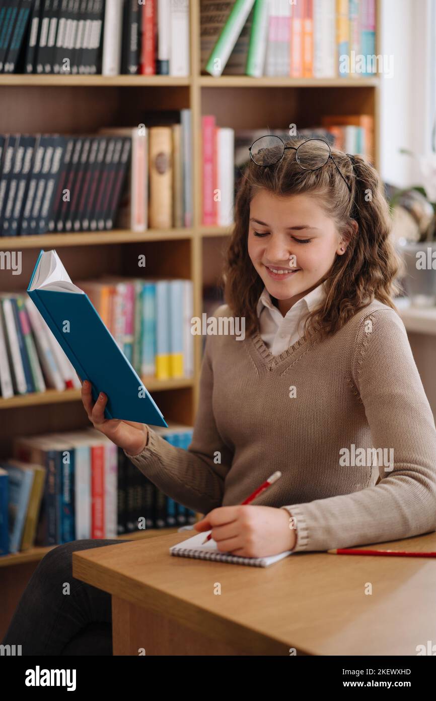 Attractive happy young girl student studying at the college library ...