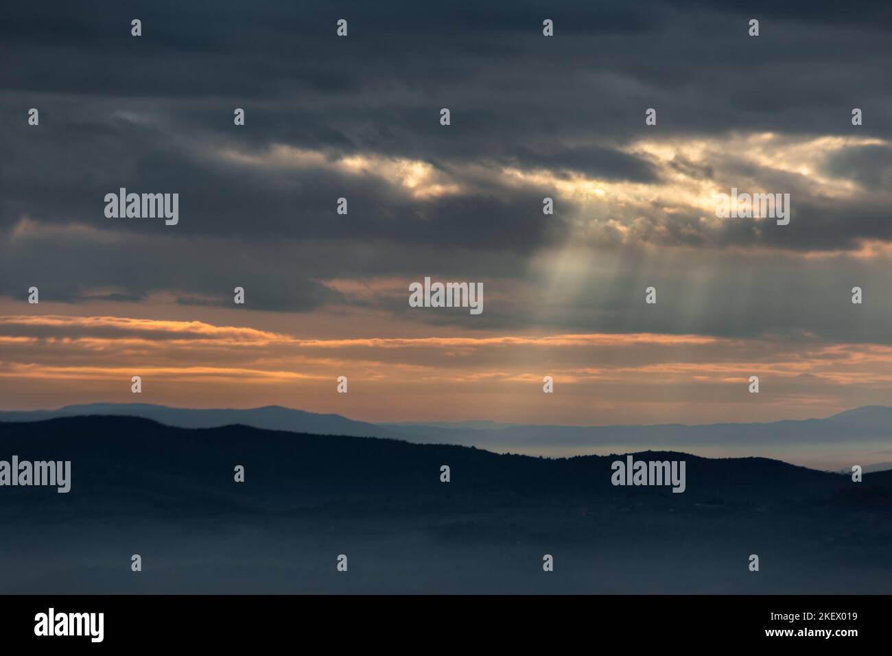 Sun rays coming down from some clouds above mountains Stock Photo - Alamy
