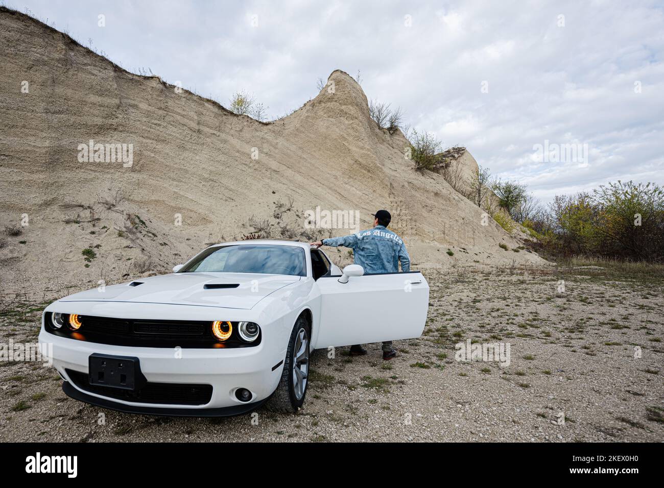 Back of man in jeans jacket and cap is standing, near his white muscle ...