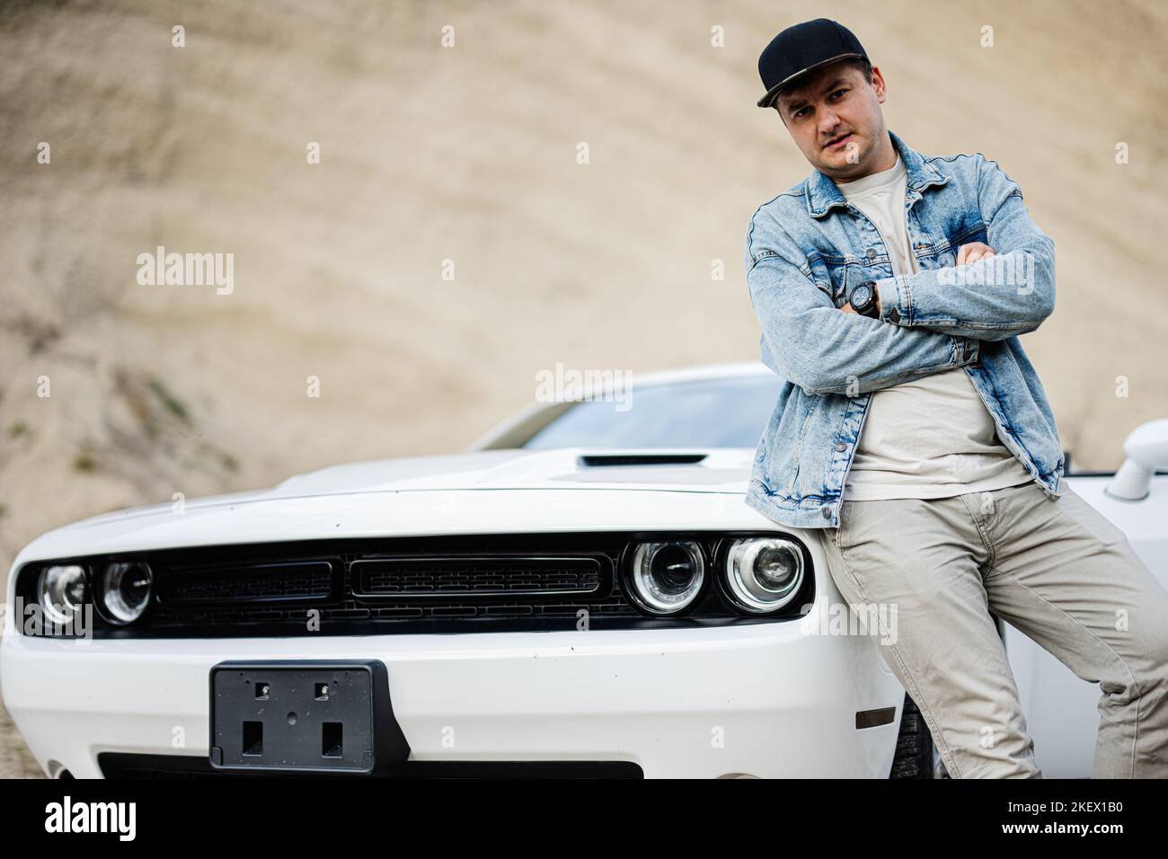 Handsome man in jeans jacket and cap is standing near his white muscle ...