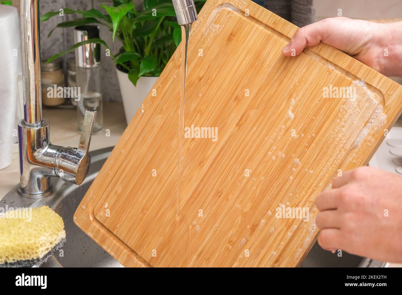 A man washes a wooden bamboo cutting board in the kitchen sink under ...