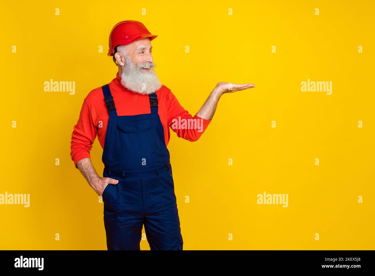 Photo of positive funky senior guy dressed uniform overall red hardhat ...