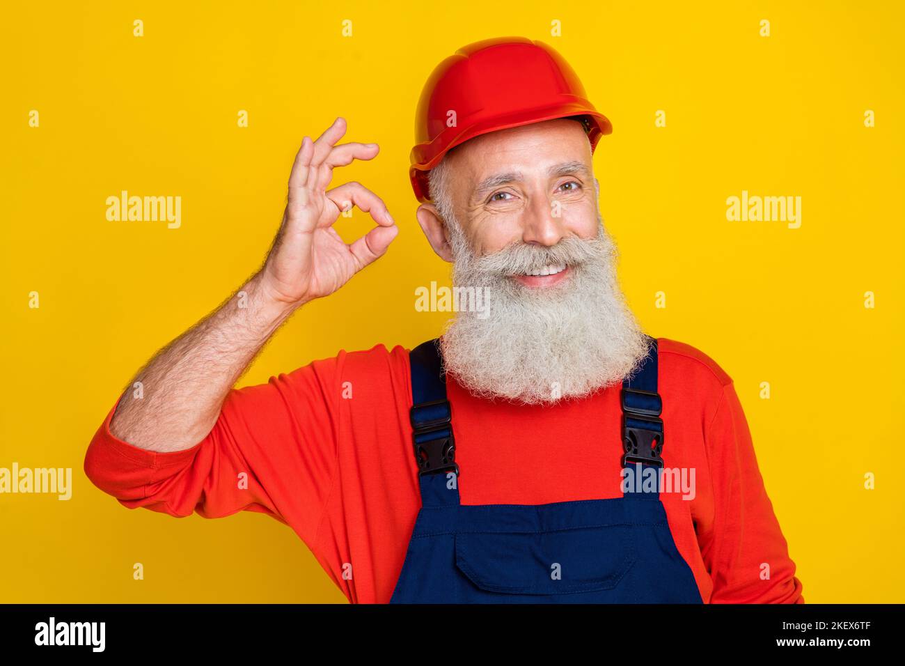 Photo of pretty cheerful senior guy dressed uniform overall red hardhat ...