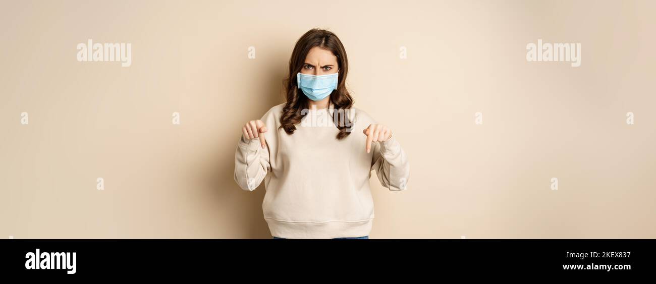Angry woman in medical face mask, pointing fingers down and looking ...