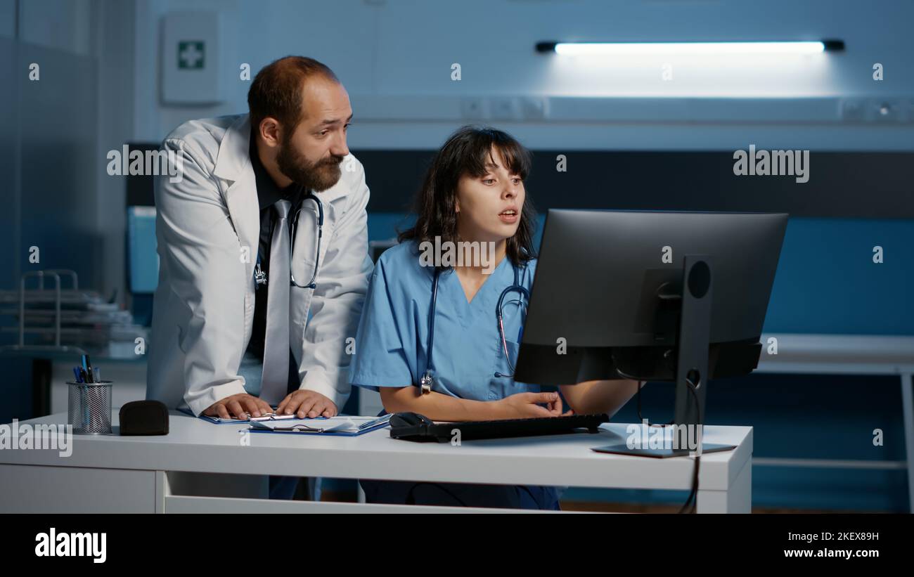 Practitioner and nurse checking medical report on computer analyzing ...