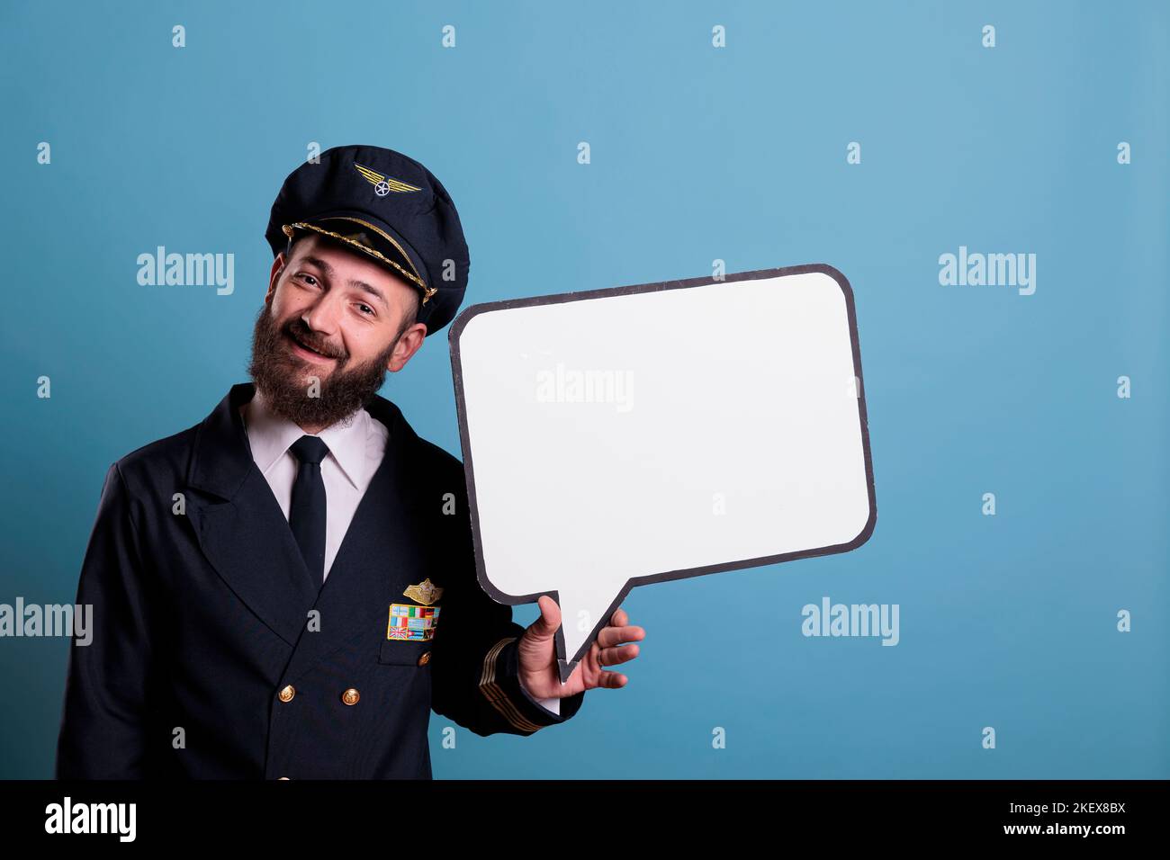 Smiling airplane pilot holding white blank speech bubble, communication ...