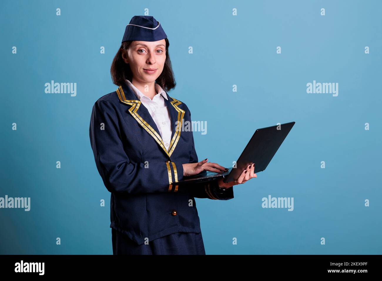 Smiling flight attendant using laptop, typing message, looking at ...