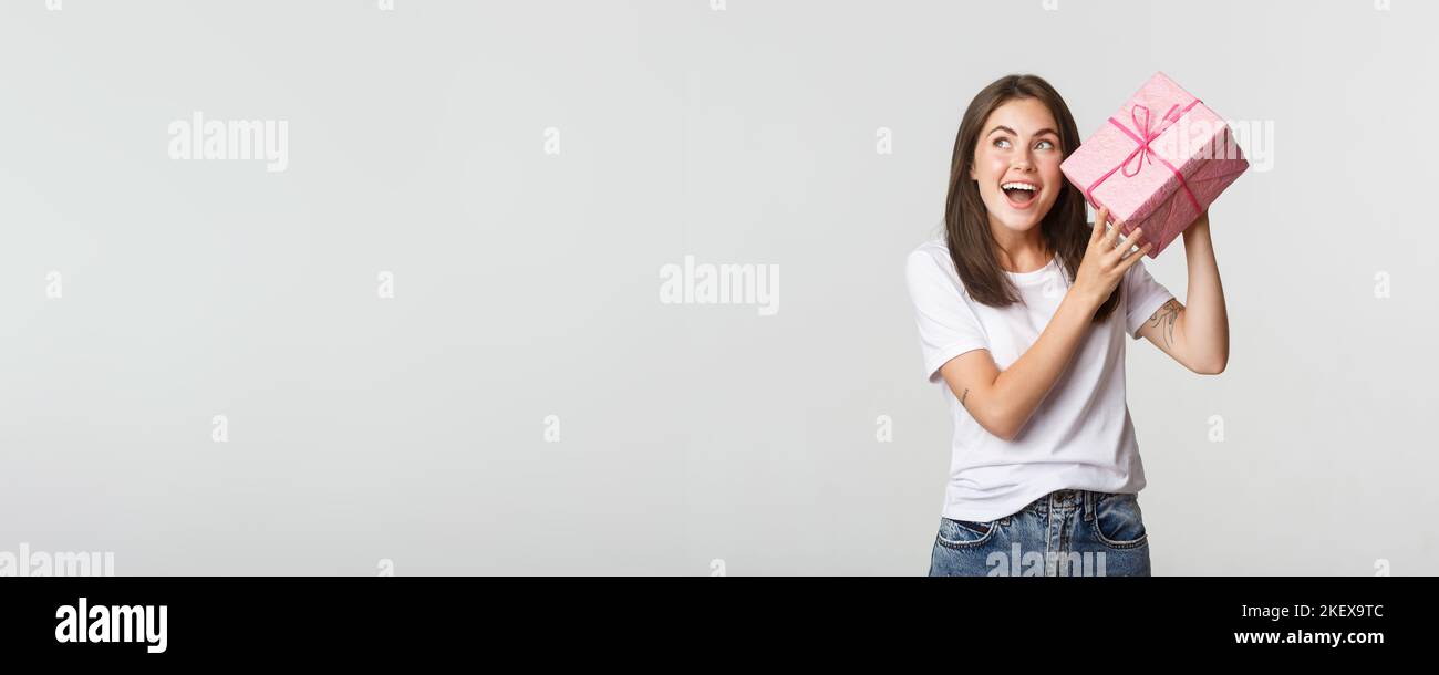 Intrigued happy birthday girl shaking gift box to find out what inside ...