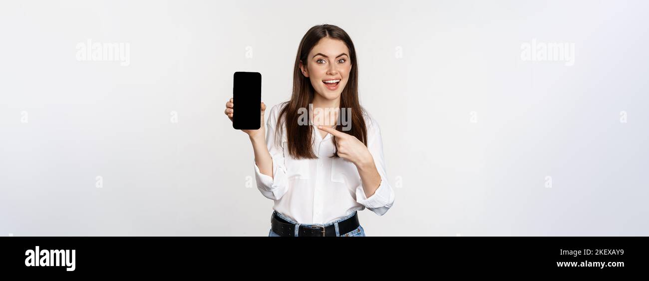 Happy beautiful woman smiling, pointing at mobile phone screen, showing ...