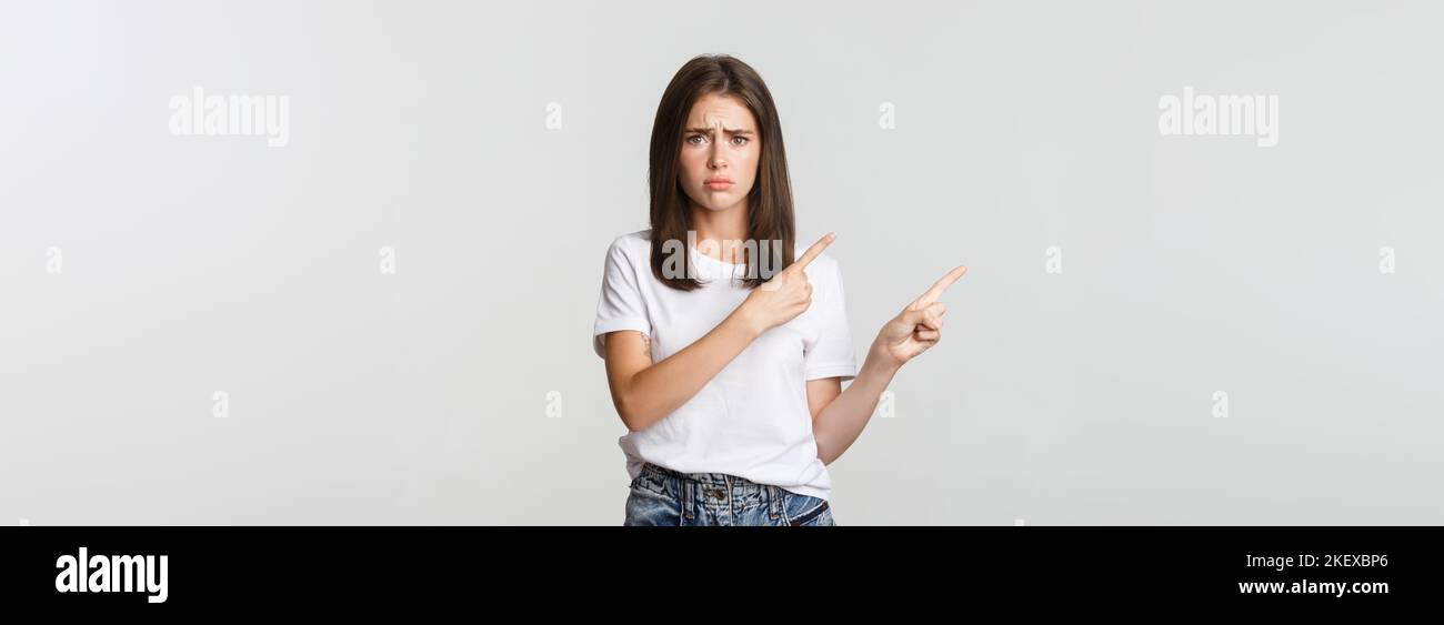Nervous timid cute girl pointing fingers upper left corner and looking ...