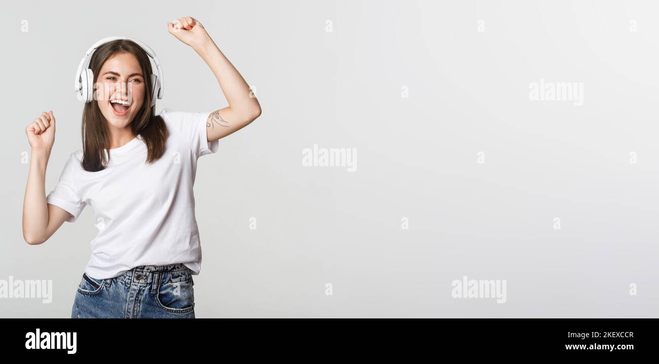 Attractive joyful girl dancing in wireless headphones, listening music ...