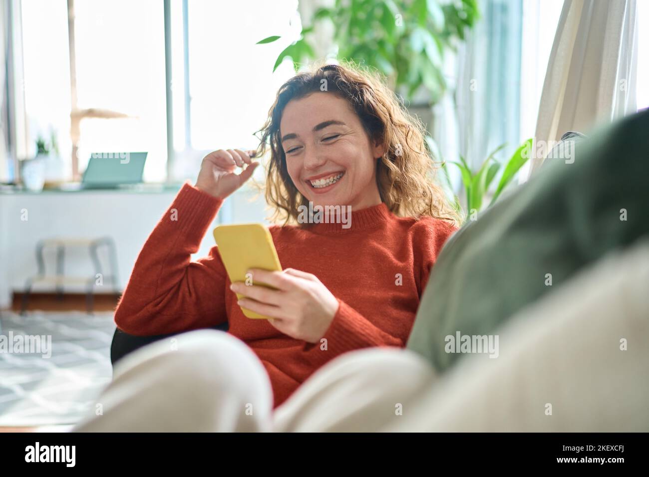 Happy relaxed young woman sitting on couch using mobile phone ...