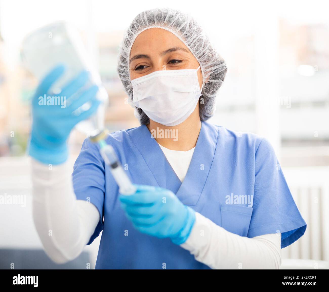 Female nurse wearing a protective mask fills a syringe with saline ...