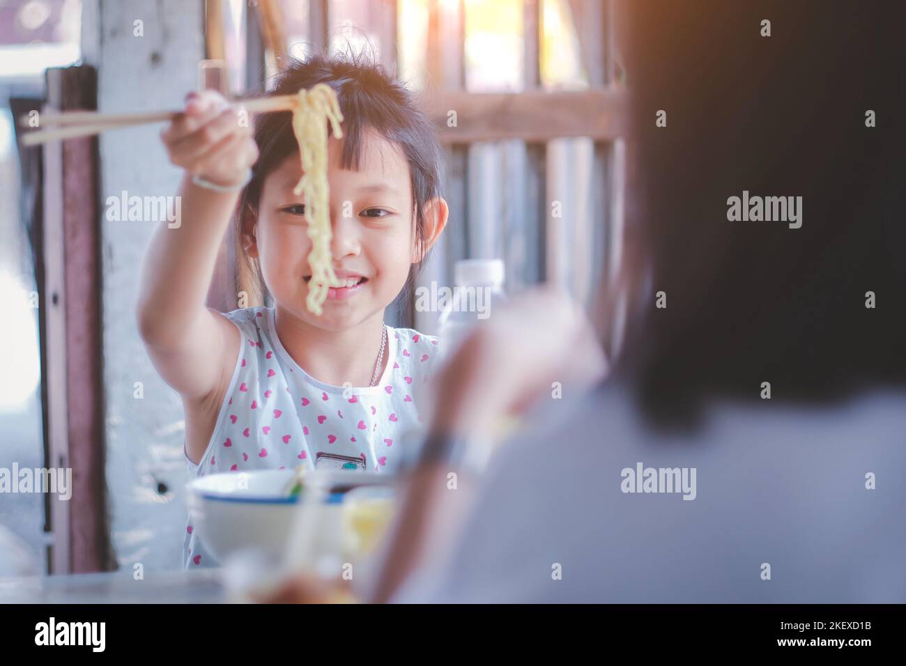 Smiling Asian girls happily eating noodles with their mother sitting ...
