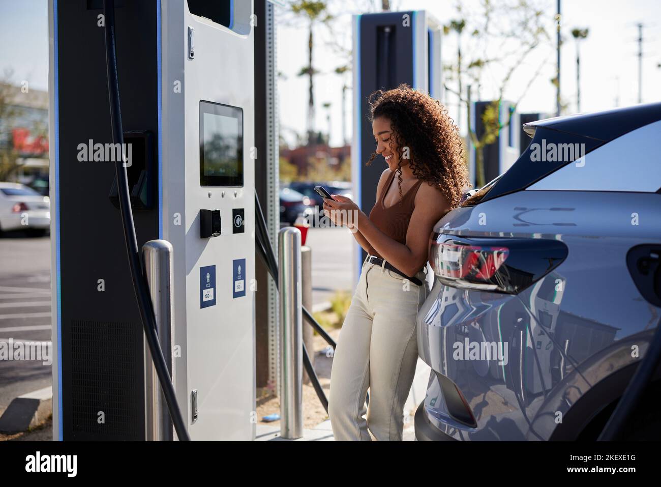 Young woman text messaging at electric vehicle charging station Stock ...