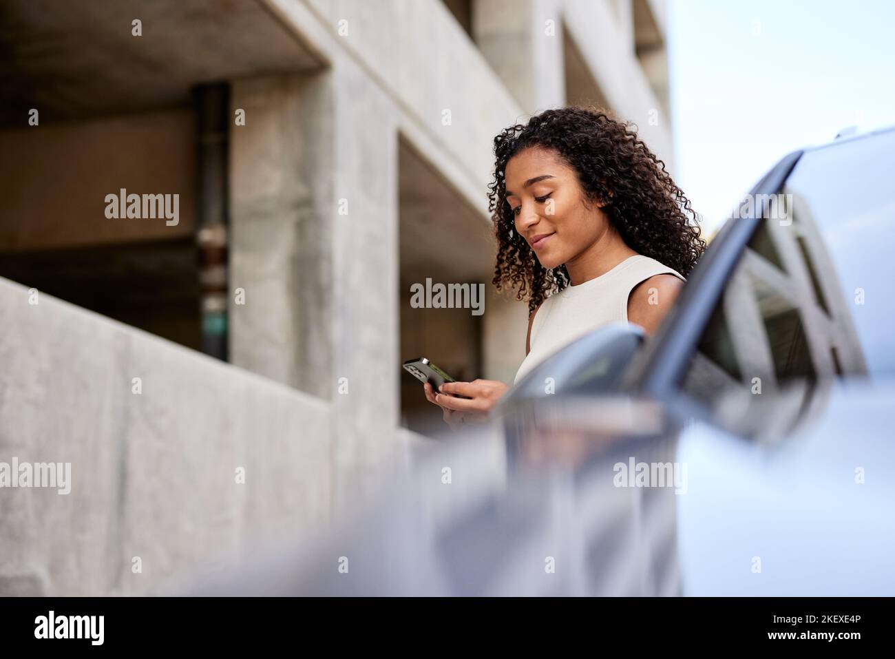 Young woman text messaging on smart phone by electric car Stock Photo ...