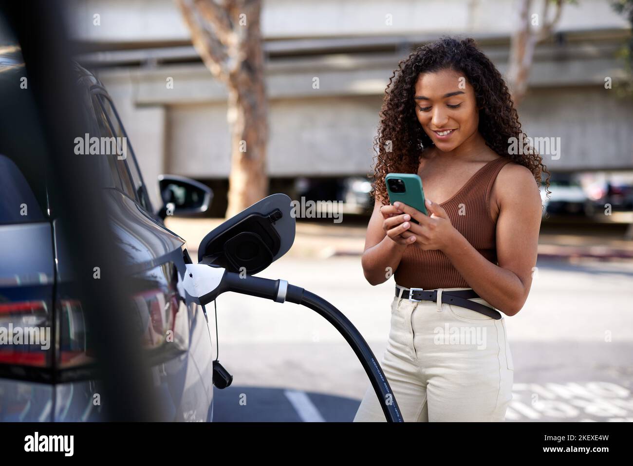 Smiling woman using smart phone by car getting charged at station Stock ...