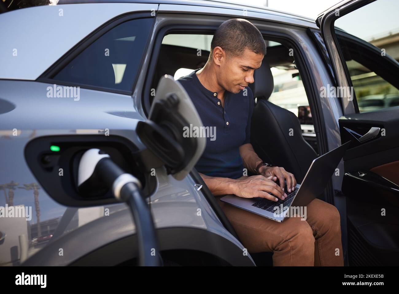 Man using laptop sitting in electric car getting charged at station ...