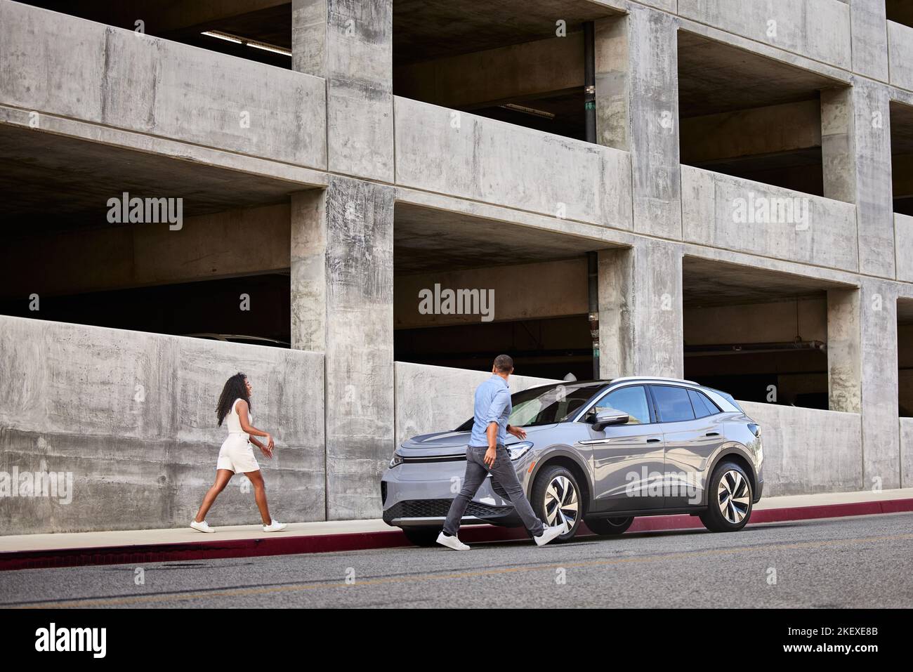 Full length of couple walking towards electric car parked on roadside ...