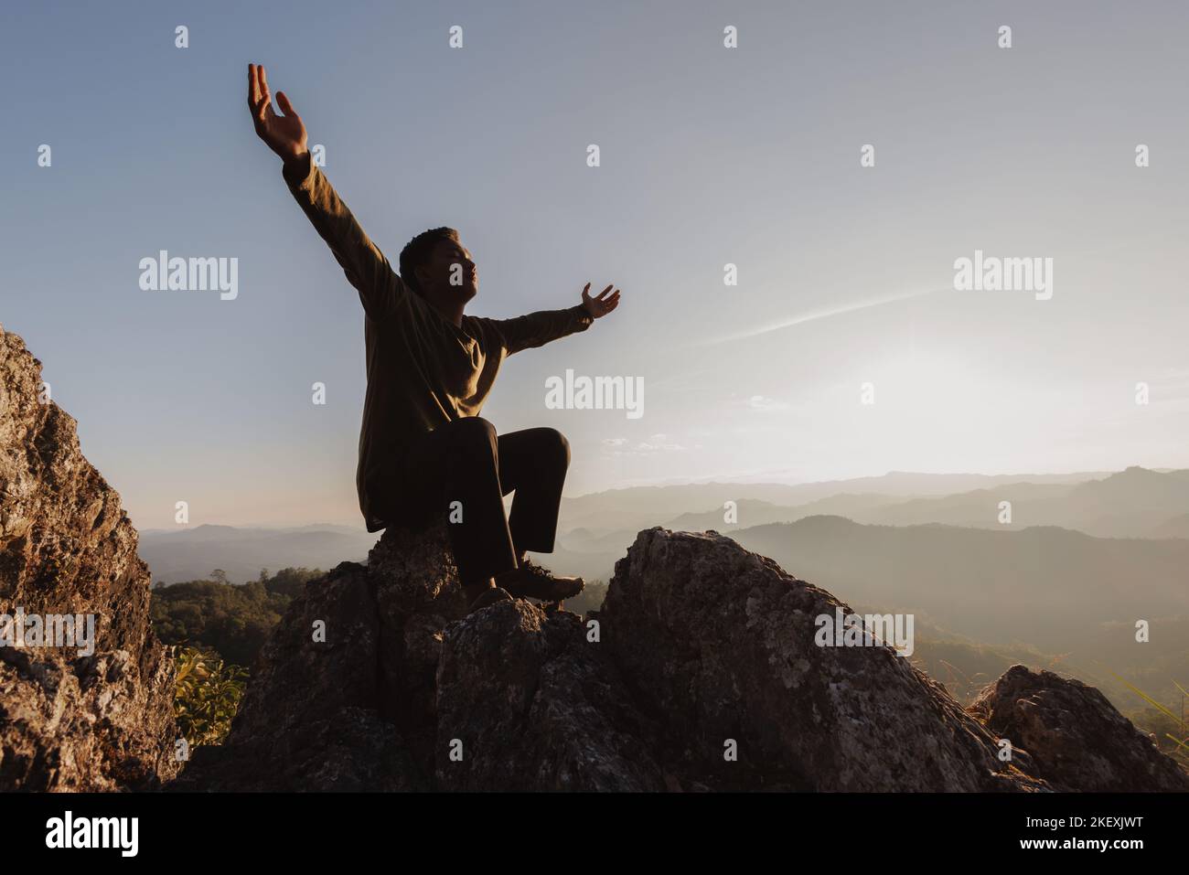 silhouette of man rise hand up praying on top of mountain and sunset ...