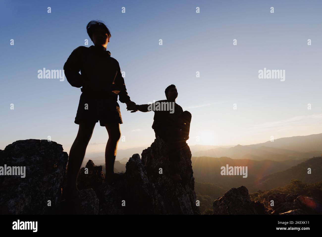 Silhouette of hiker helping each other hike up a mountain at sunset ...
