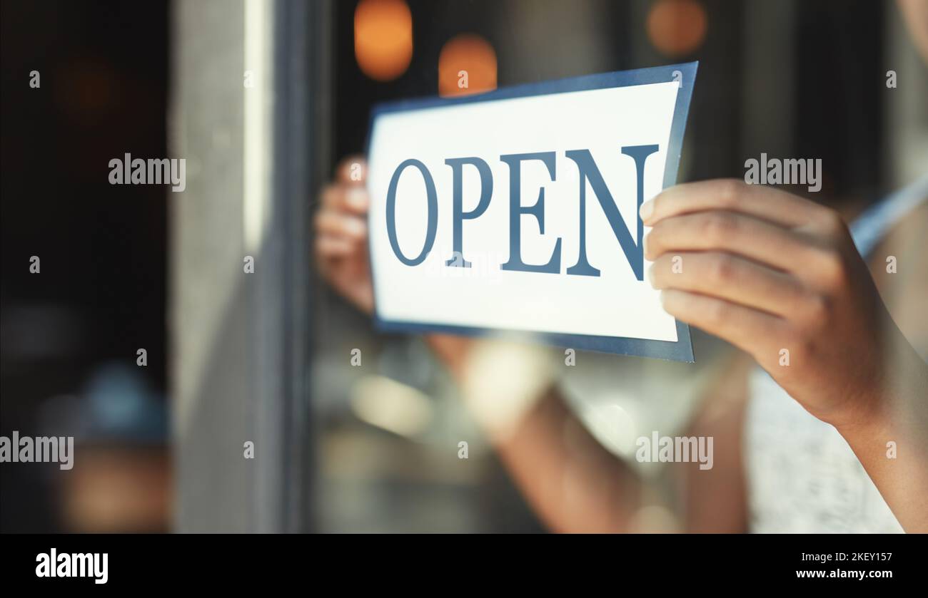 Ready for her very first customer. a woman hanging up an open sign on ...