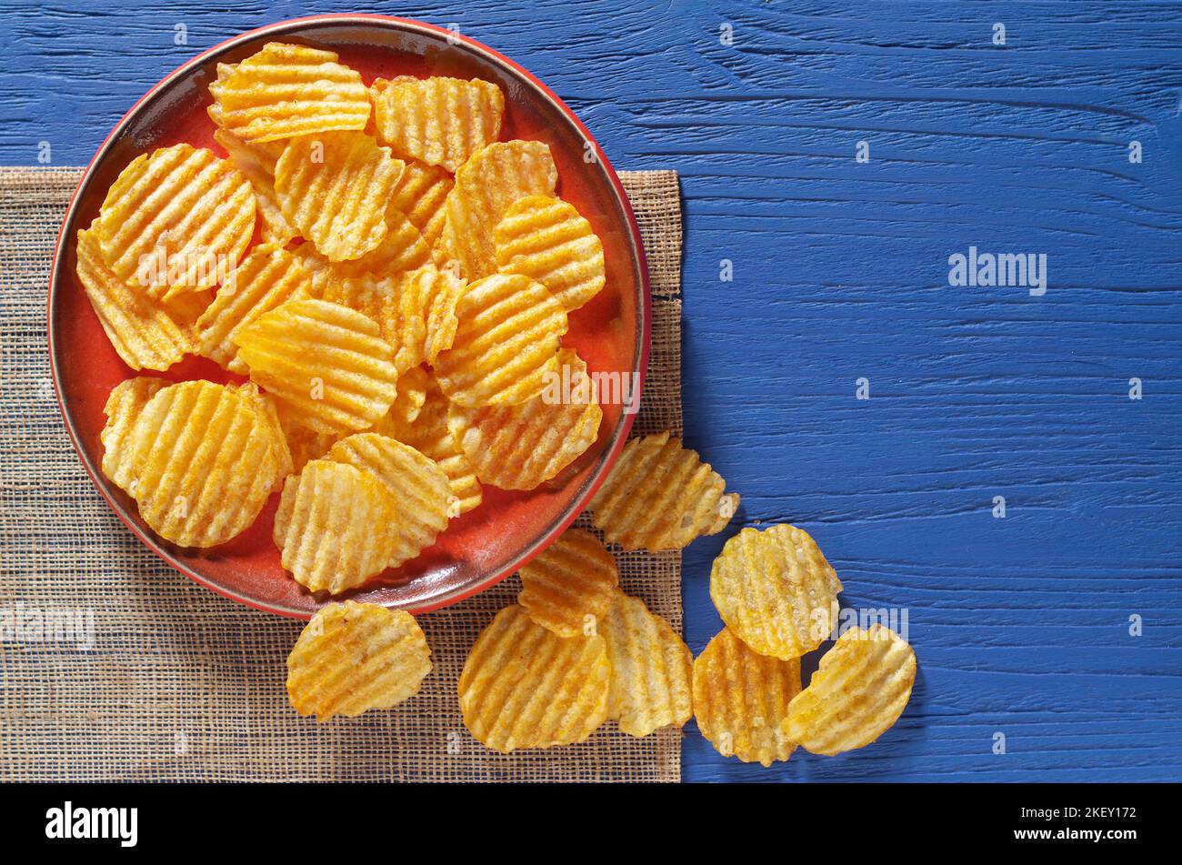 Salty potato crisps in red plate on blue wooden table, top view with ...