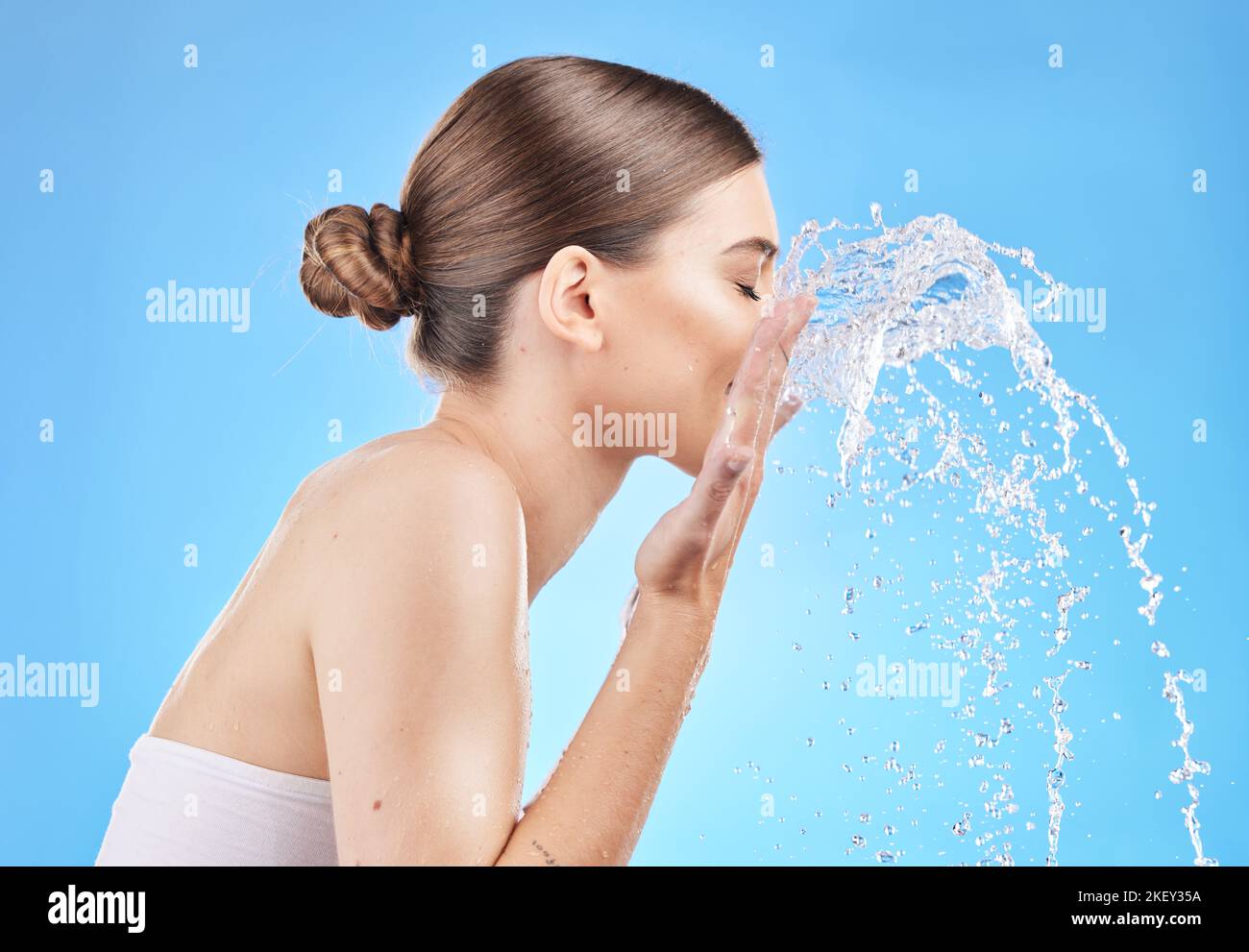 Skincare, water and woman cleaning face in studio on blue background ...
